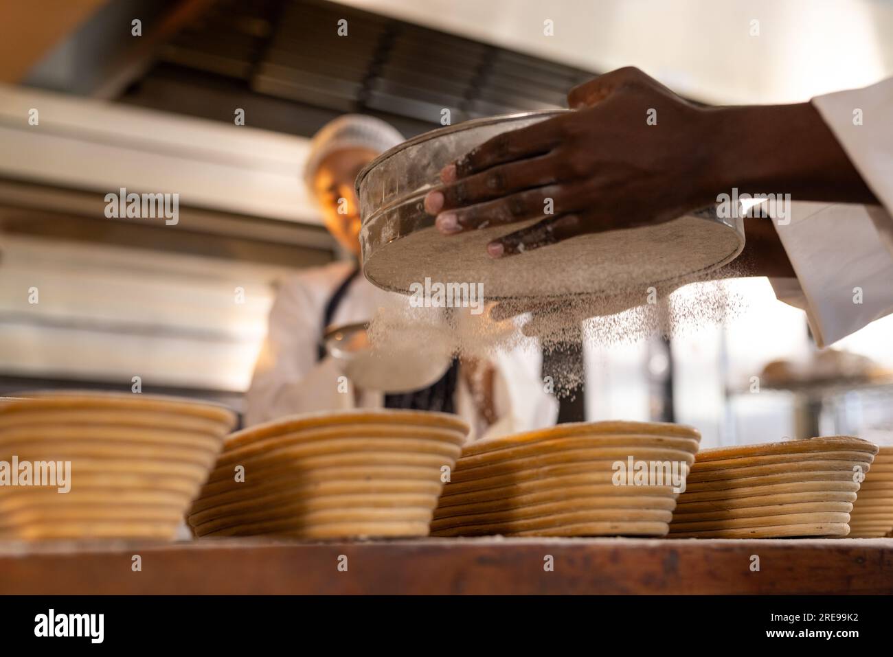 Diverse bakers wearing aprons in bakery kitchen and pouring flour on ...