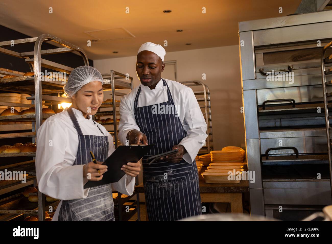Focused diverse bakers wearing aprons in bakery kitchen, holding ...