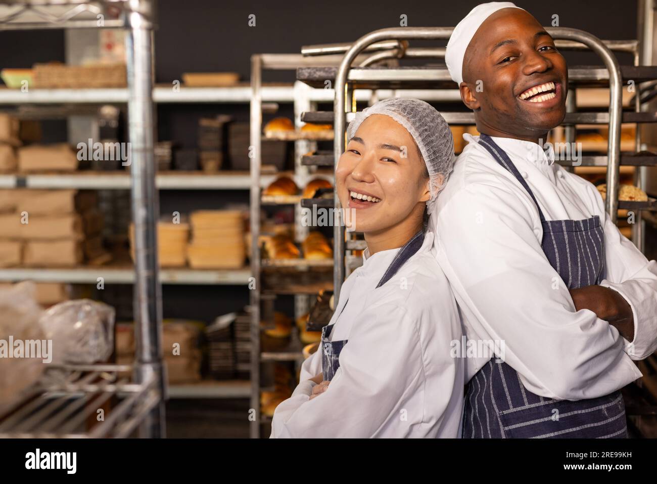 Portrait of happy diverse bakers wearing aprons in bakery with arms ...