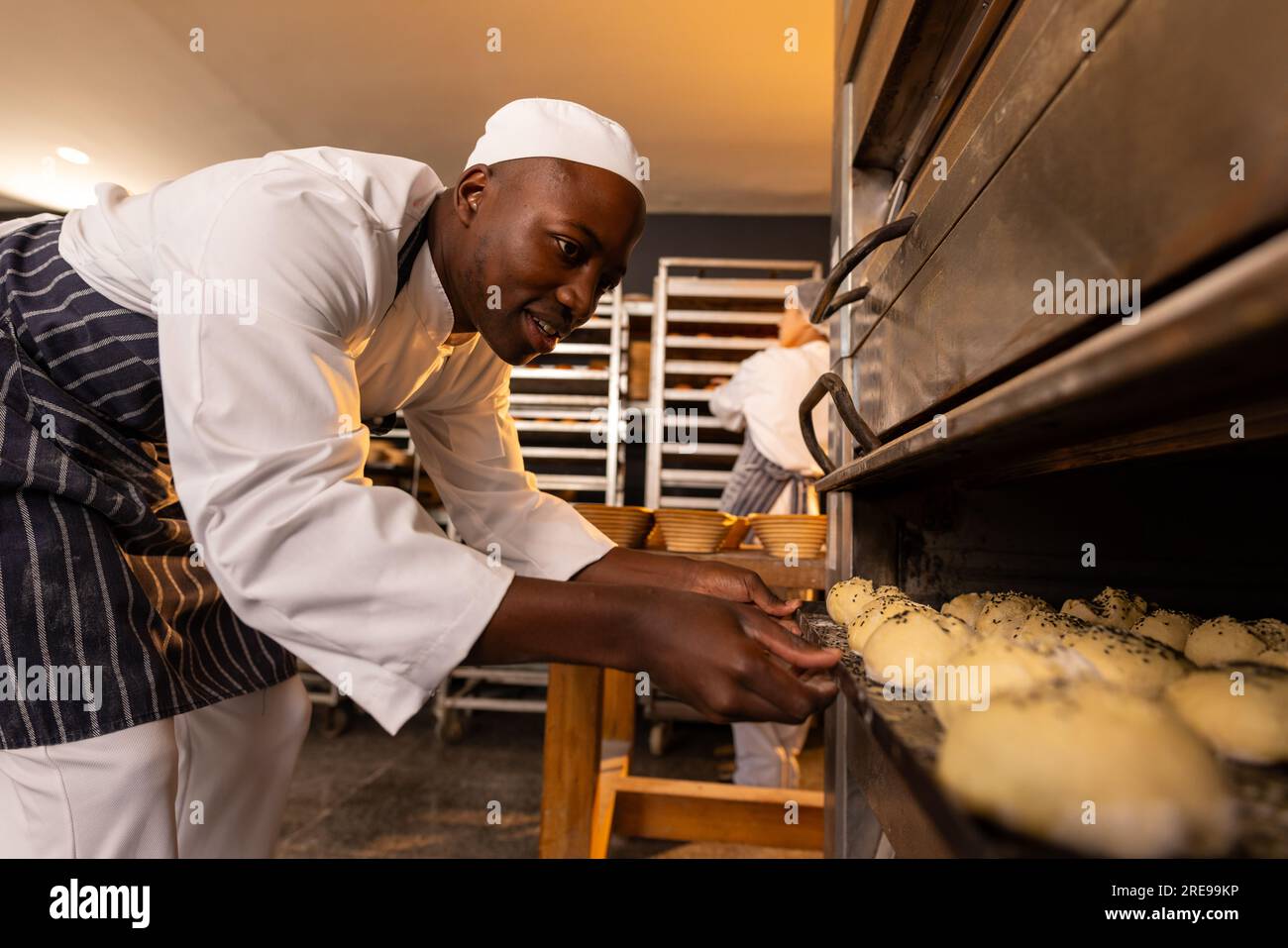 Happy diverse bakers wearing aprons in bakery kitchen and baking rolls ...