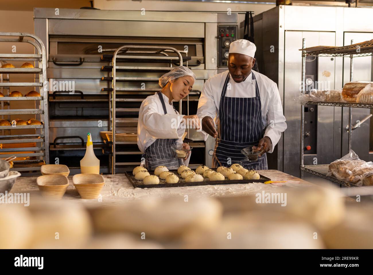 Focused diverse bakers wearing aprons in bakery kitchen and sprinkling ...