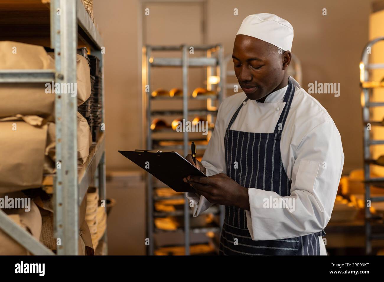 Focused african american male baker in bakery kitchen writing on ...