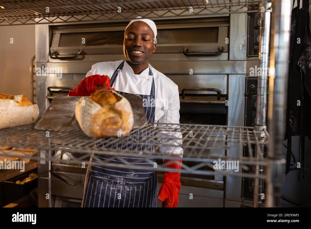 Happy african american male baker in bakery kitchen taking fresh bread ...