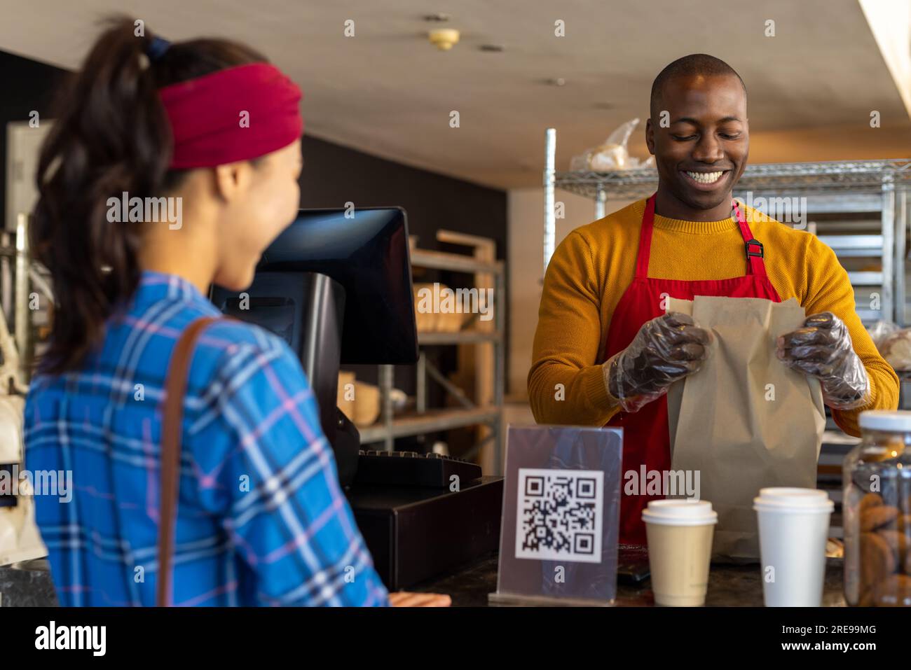 Happy diverse customer and male bakery worker packing order in paper ...