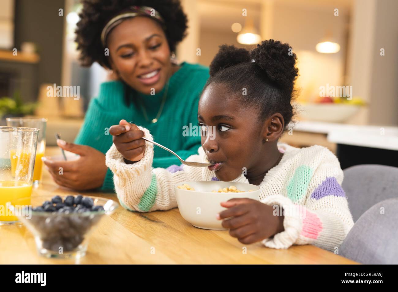 Happy african american mother and daughter sitting at table eating ...