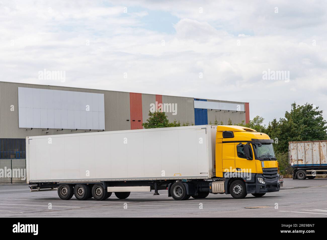 A large semi-trailer with a yellow cab stands near an industrial ...
