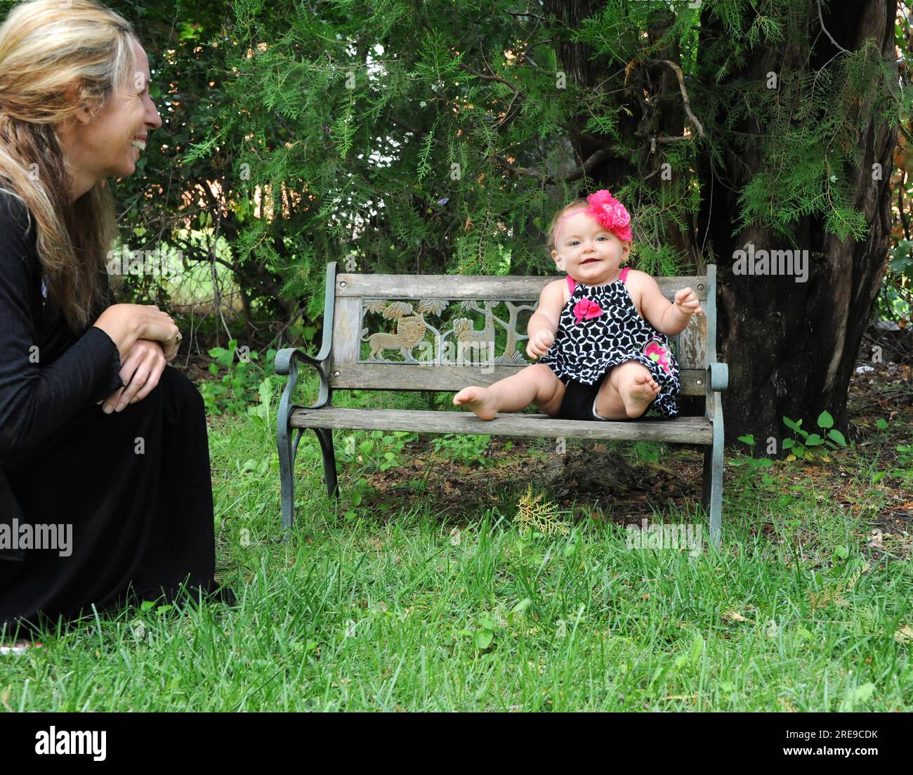 Mother looks on with pride as baby daughter sits sweetly on park bench ...