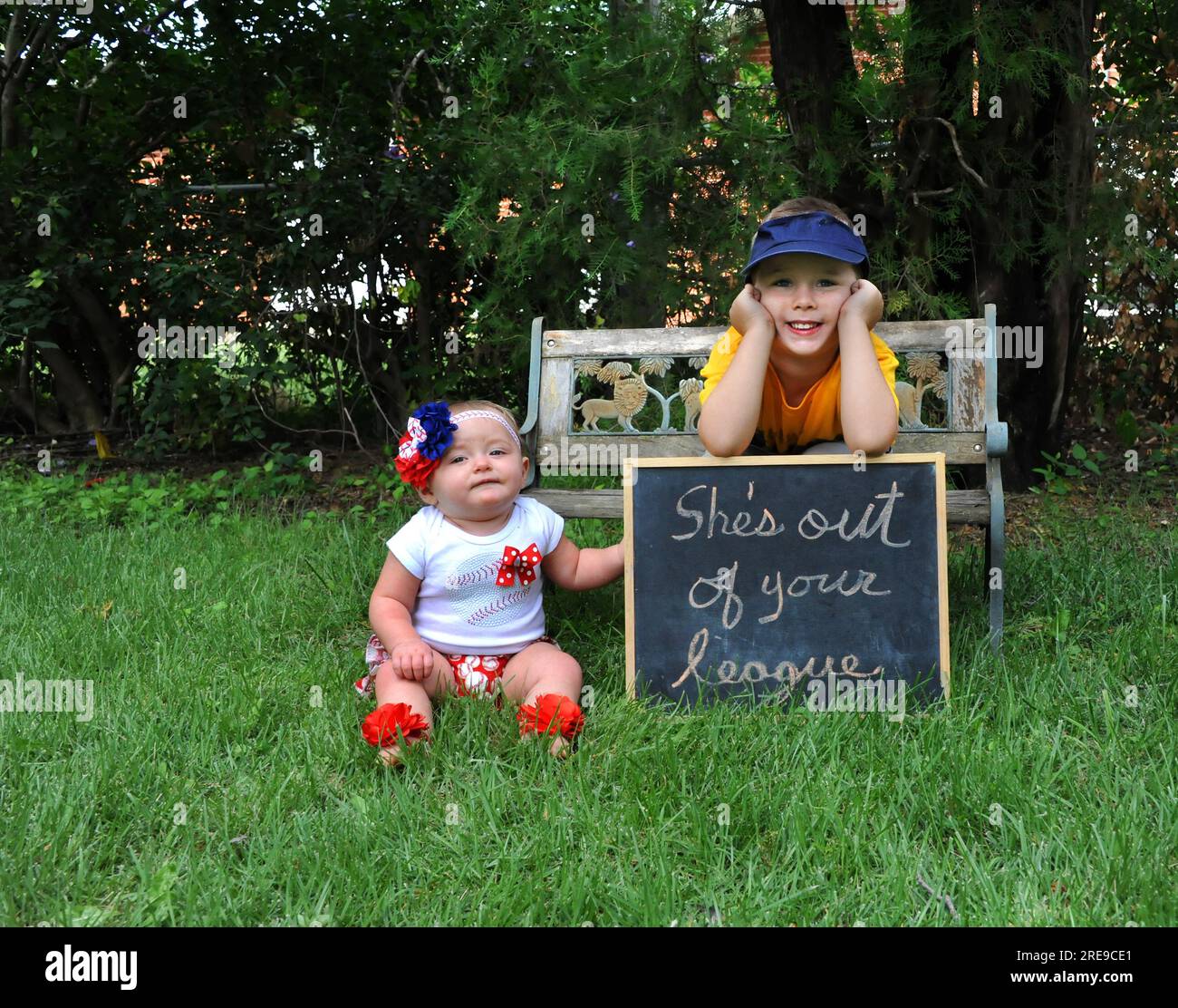 Baby sister and big brother pose besides sign reading "She is out of ...