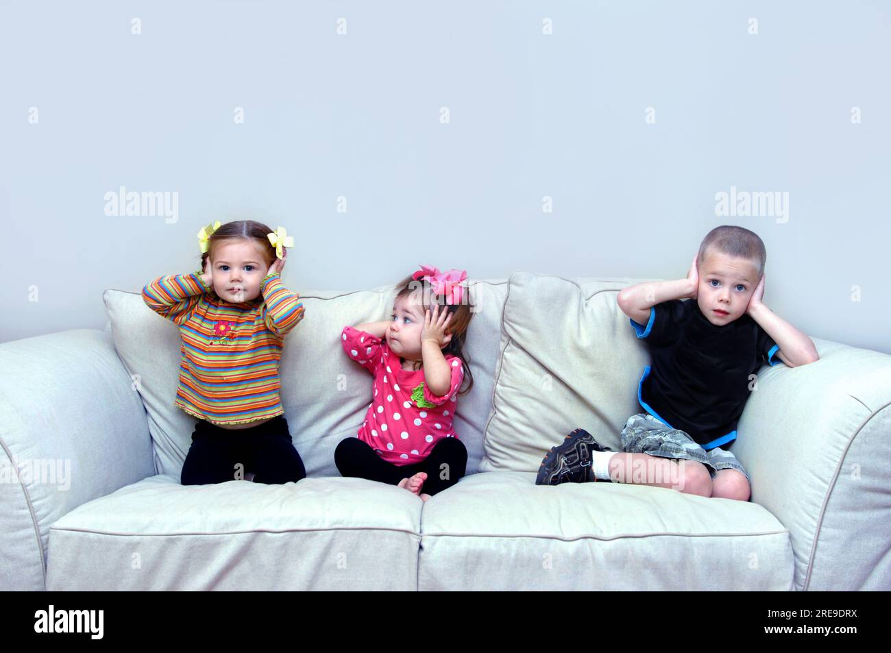 Three children sit on a couch in their home. They are covering their ...