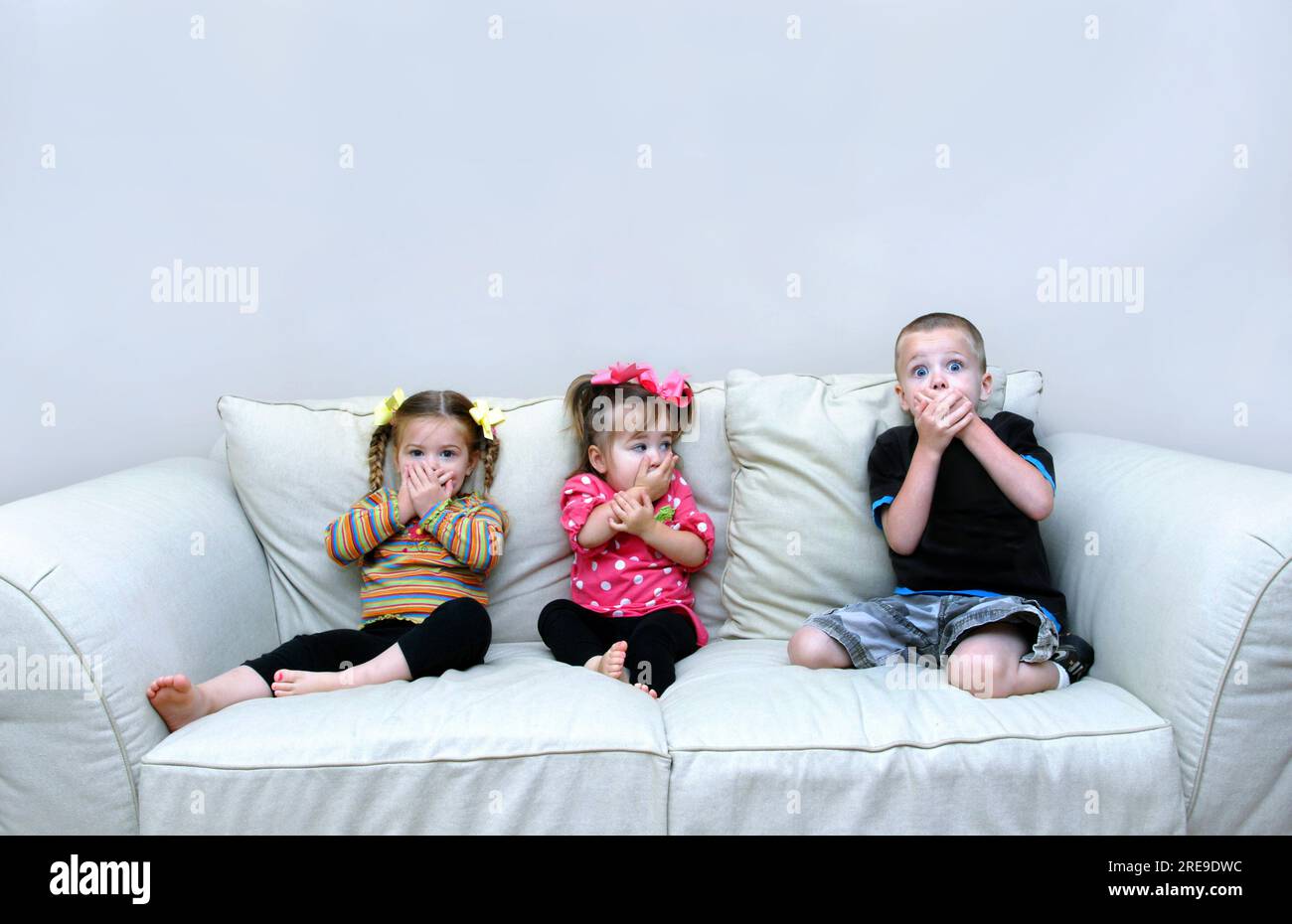 Three small children sit on a couch in their home, and cover their ...