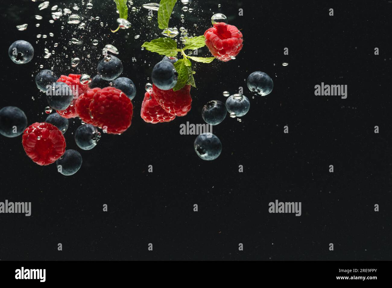 Close up of fresh berries falling into water with copy space on black ...