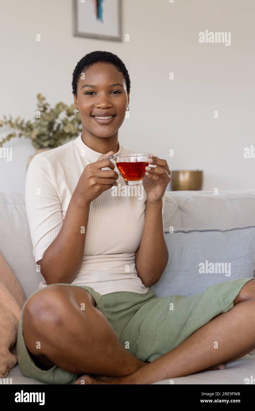 Portrait of happy african american woman sitting on sofa, holding cup ...