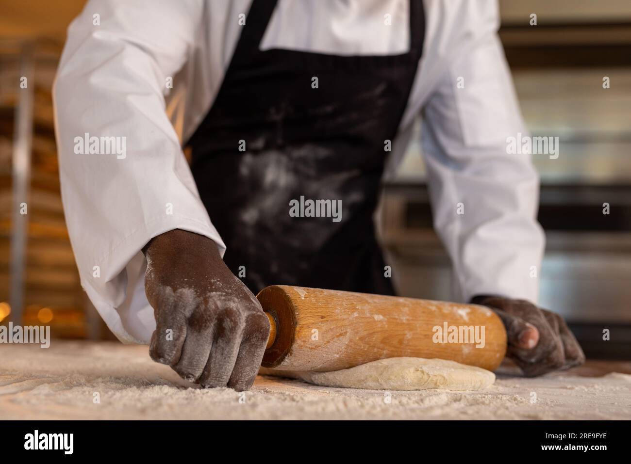 African american male baker wearing apron in bakery kitchen and rolling ...
