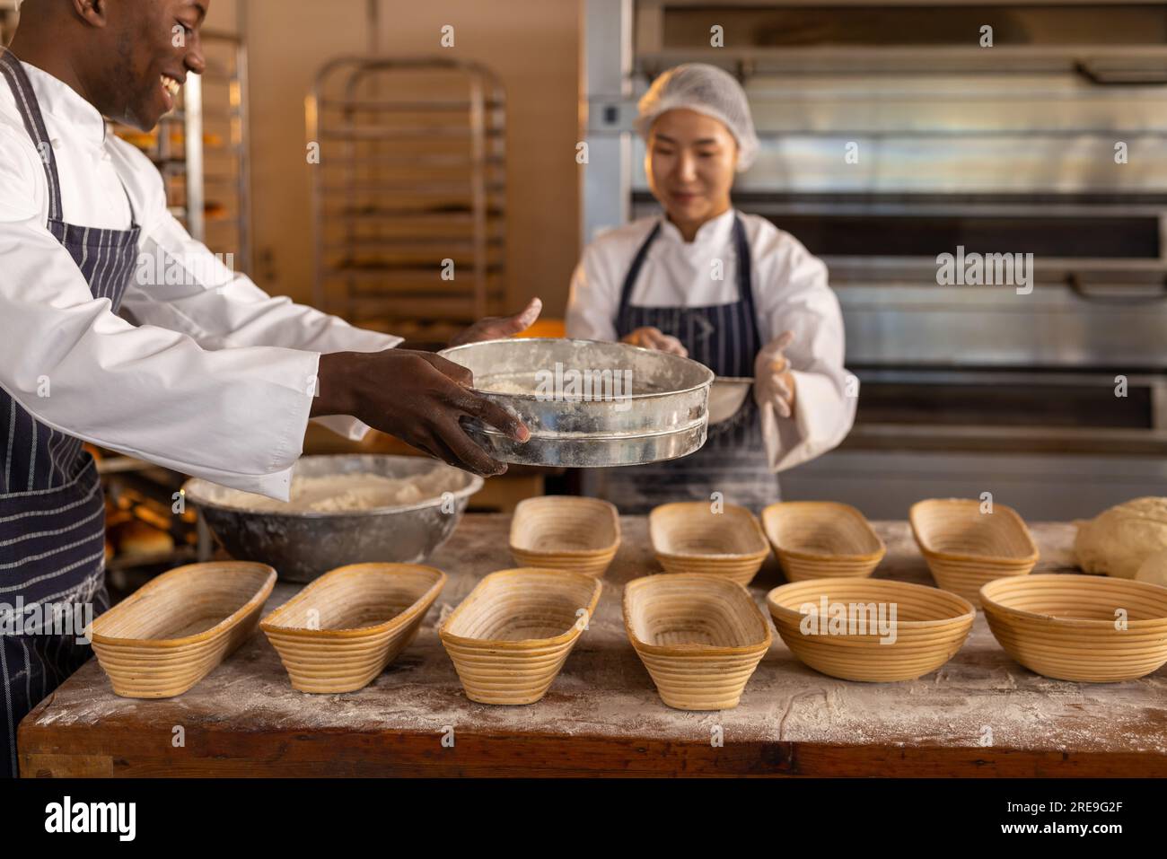 Happy diverse bakers wearing aprons in bakery kitchen and pouring flour ...