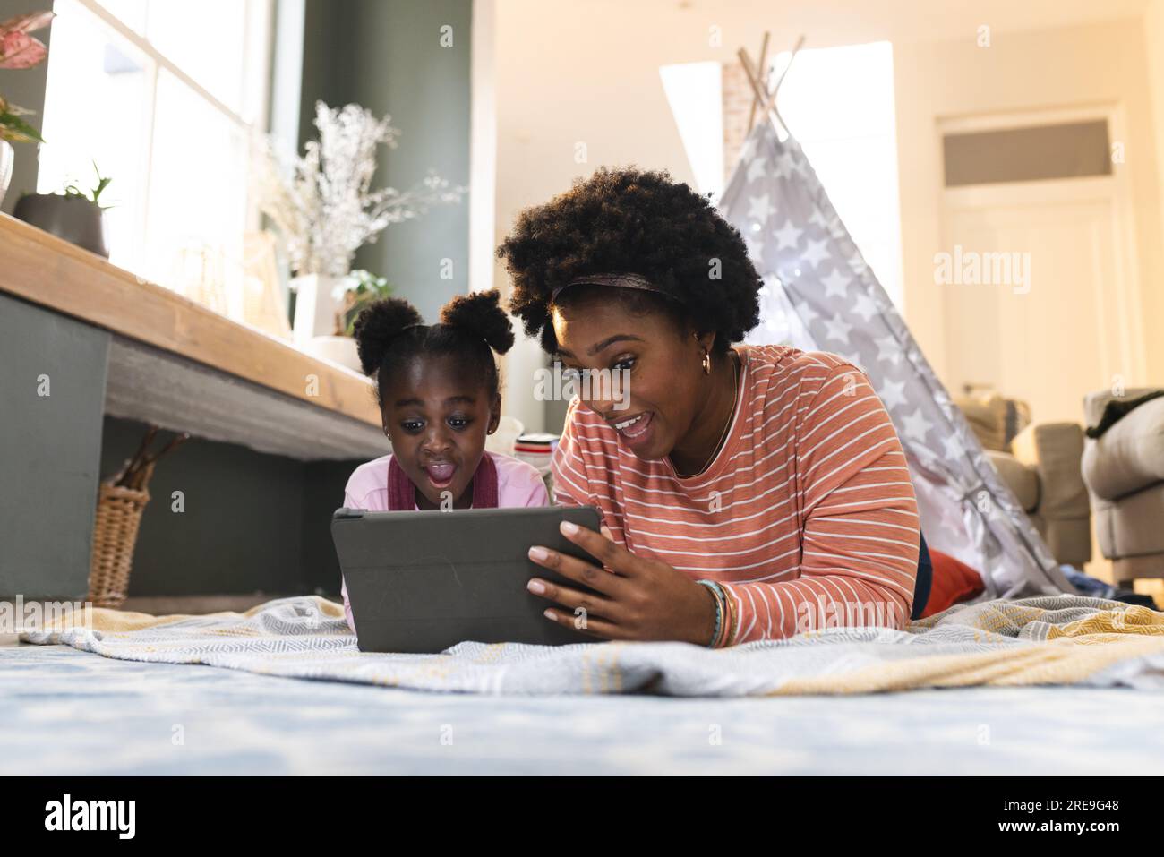Happy african american mother and daughter playing in tent, using tablet at home Stock Photo - Alamy
