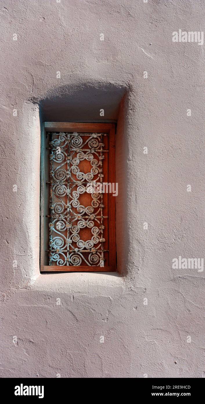 Fancy scrolled window has metal grate. Window is inset in adobe home ...