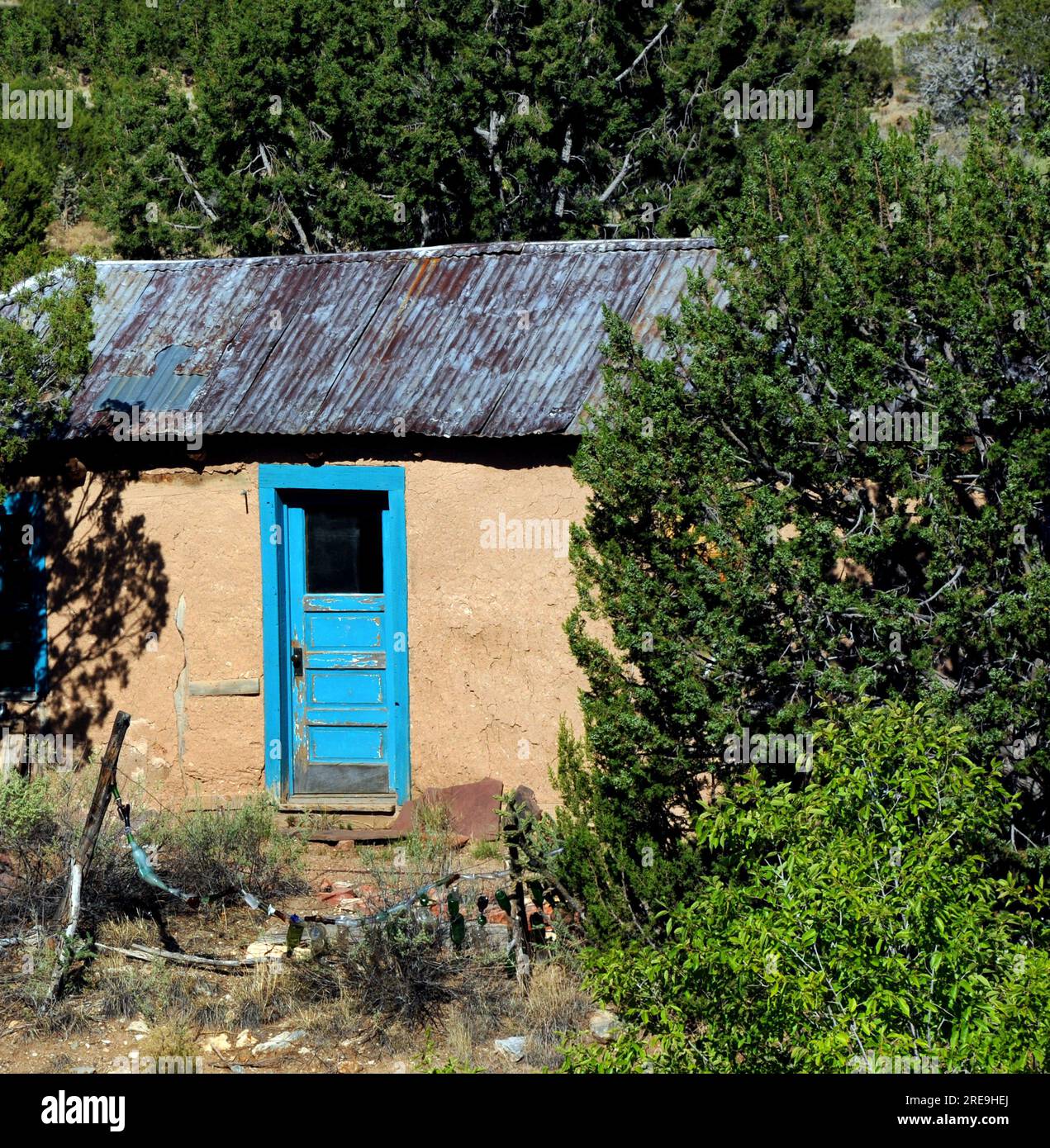 Old adobe home has weathered wooden, turquoise door. Bottle gate keeps ...