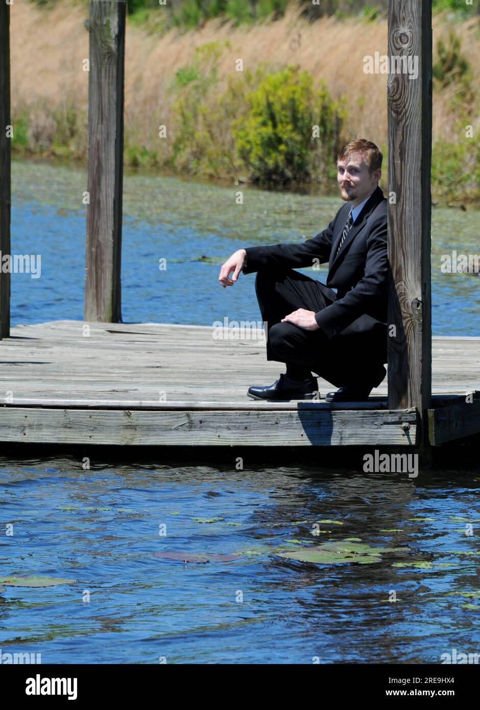 Handsome young man relaxes on a wooden dock. Lake water is blue and ...