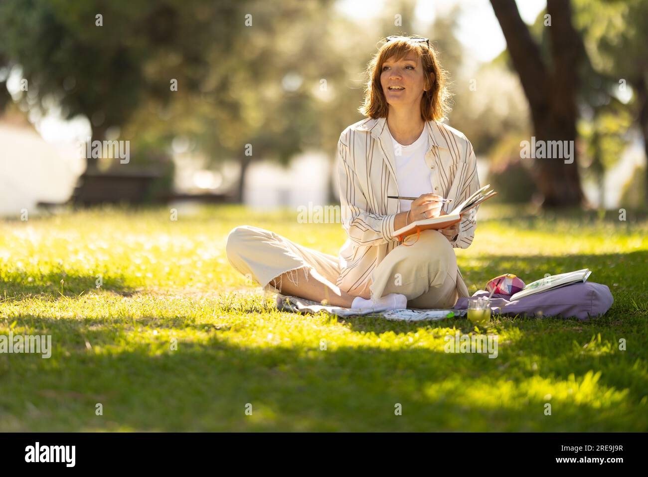 Adult smiling woman painting in her notebook in the blooming park ...