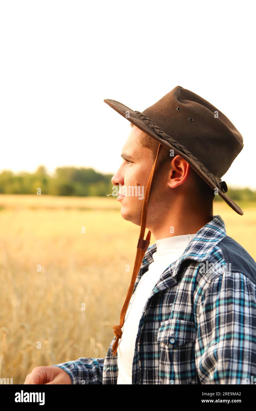A young farmer in a cowboy hat stands proudly in an agricultural field ...