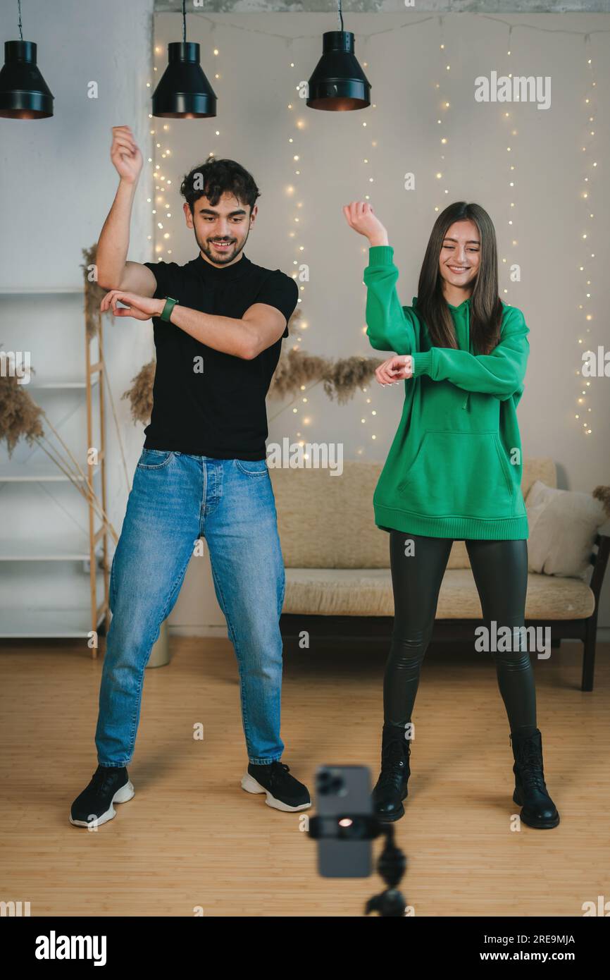 Smiling millennial blogger couple standing in living room dancing while ...