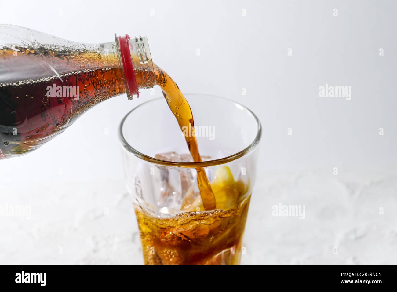 Pouring fresh cola from a bottle into a drinking glass with ice cubes and lemon slice ...