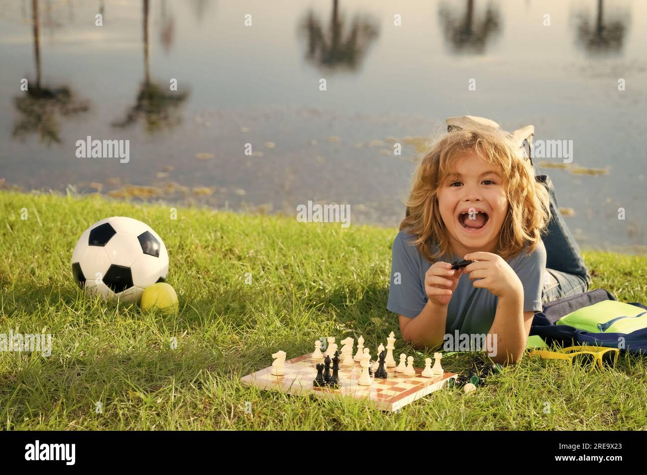 Excited kid playing chess game in backyard, laying on grass ...