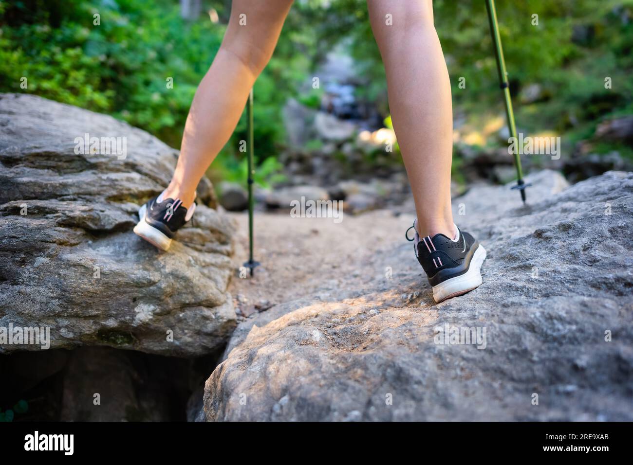 Women's legs hiking between large stones that lead to a stream in the ...