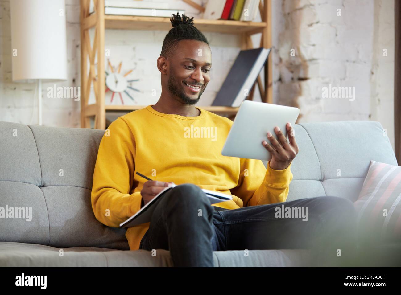 Young smiling african man, student sitting on sofa in living room at ...