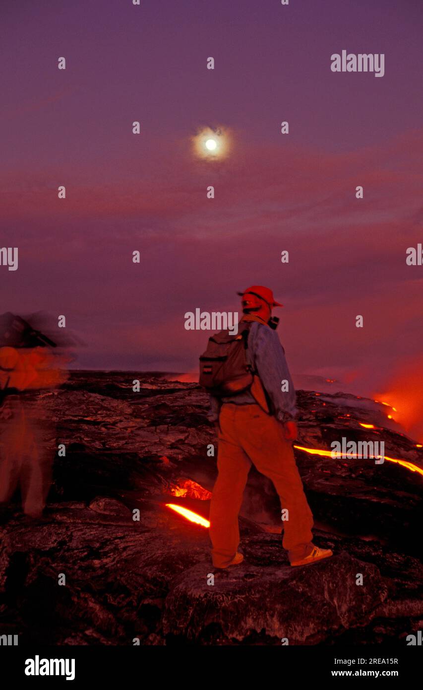 Two people standing on lava fields at Kilauea Volcano with the sun ...