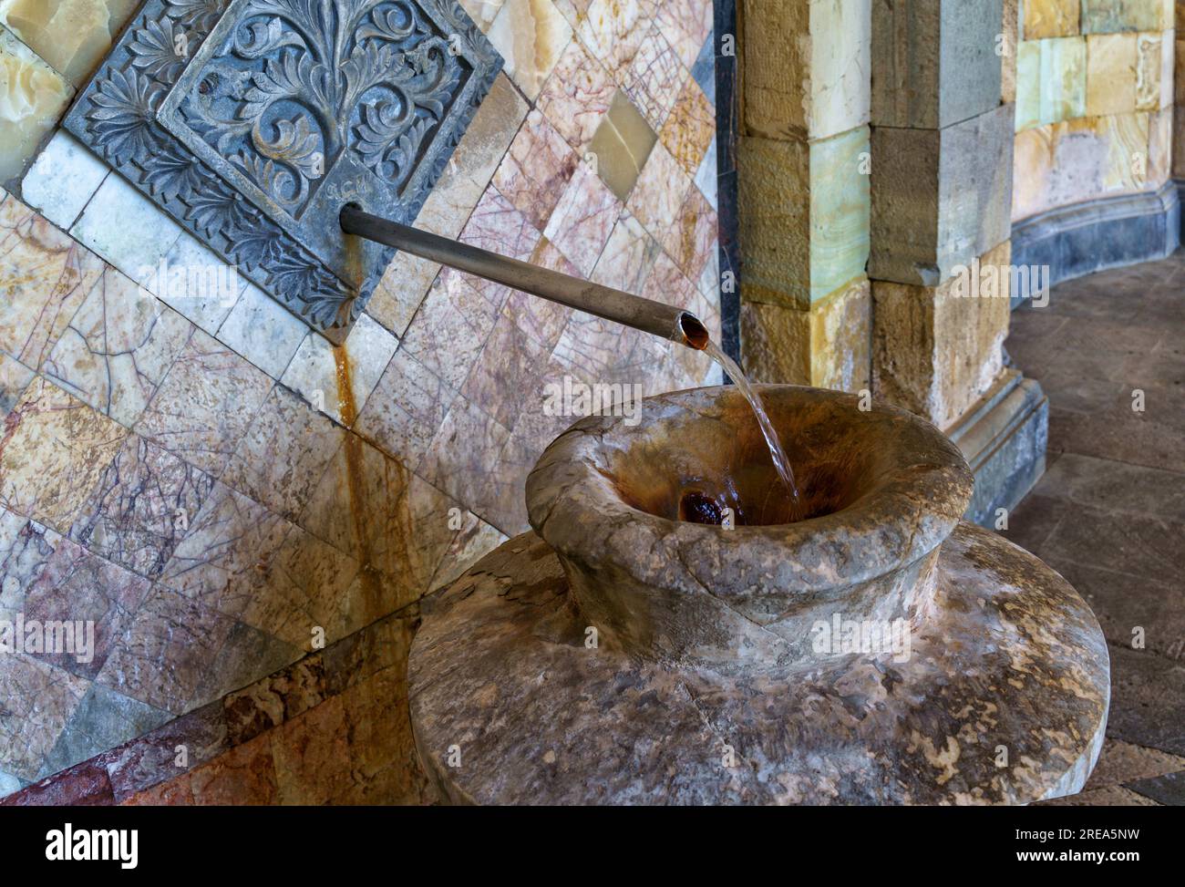 Water flows down a thin pipe into a large stone jug in the gallery of mineral water in the ...