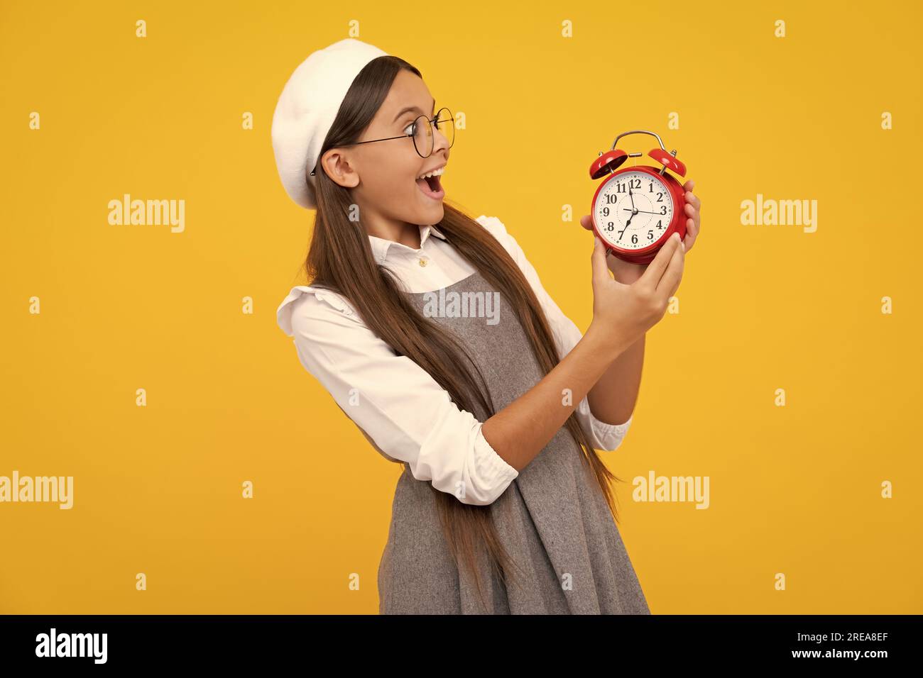 Teenager child hold clock isolated on yellow studio background ...