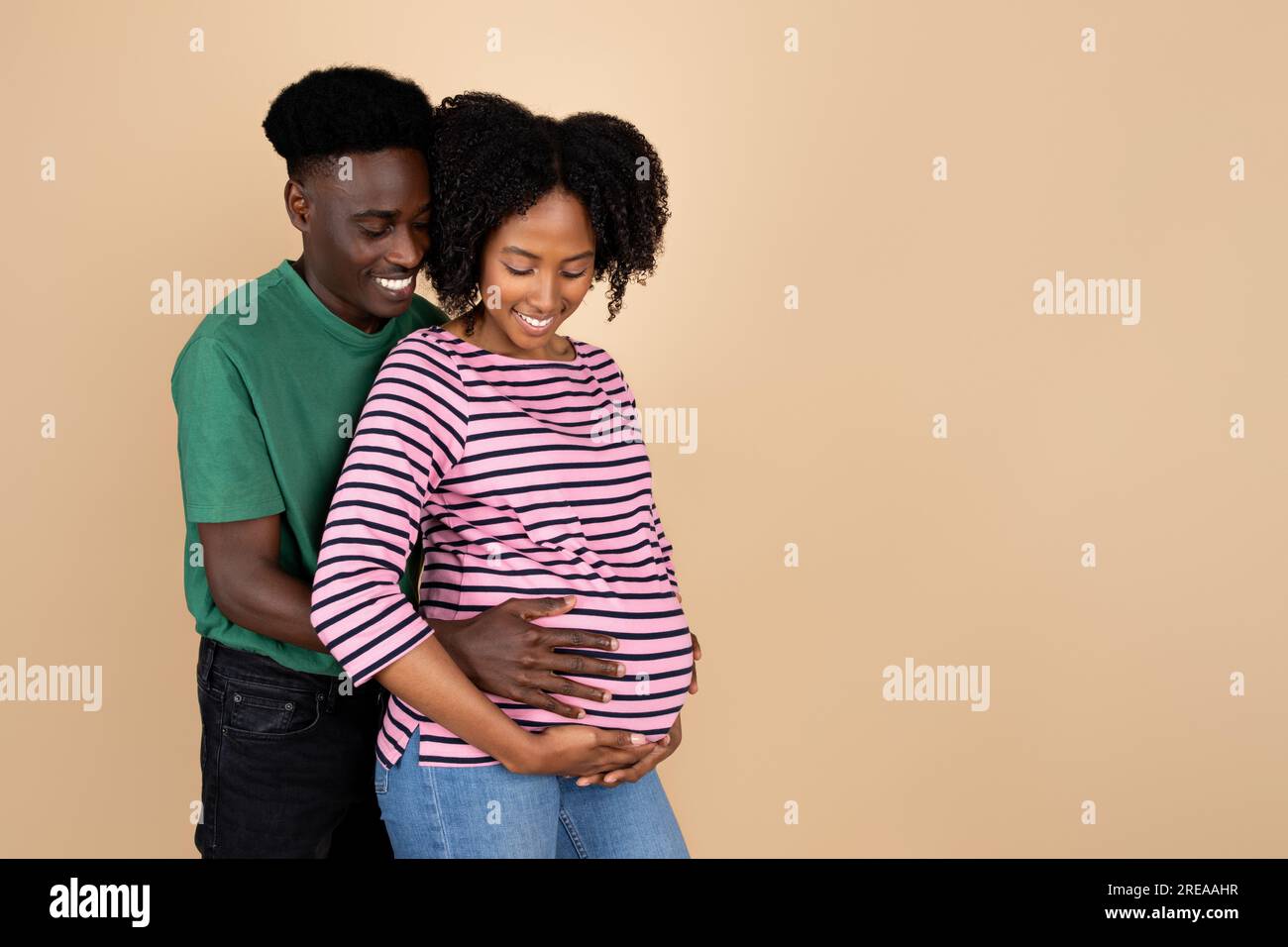 Cheerful young black man hugging lady with big belly, feel movement of ...