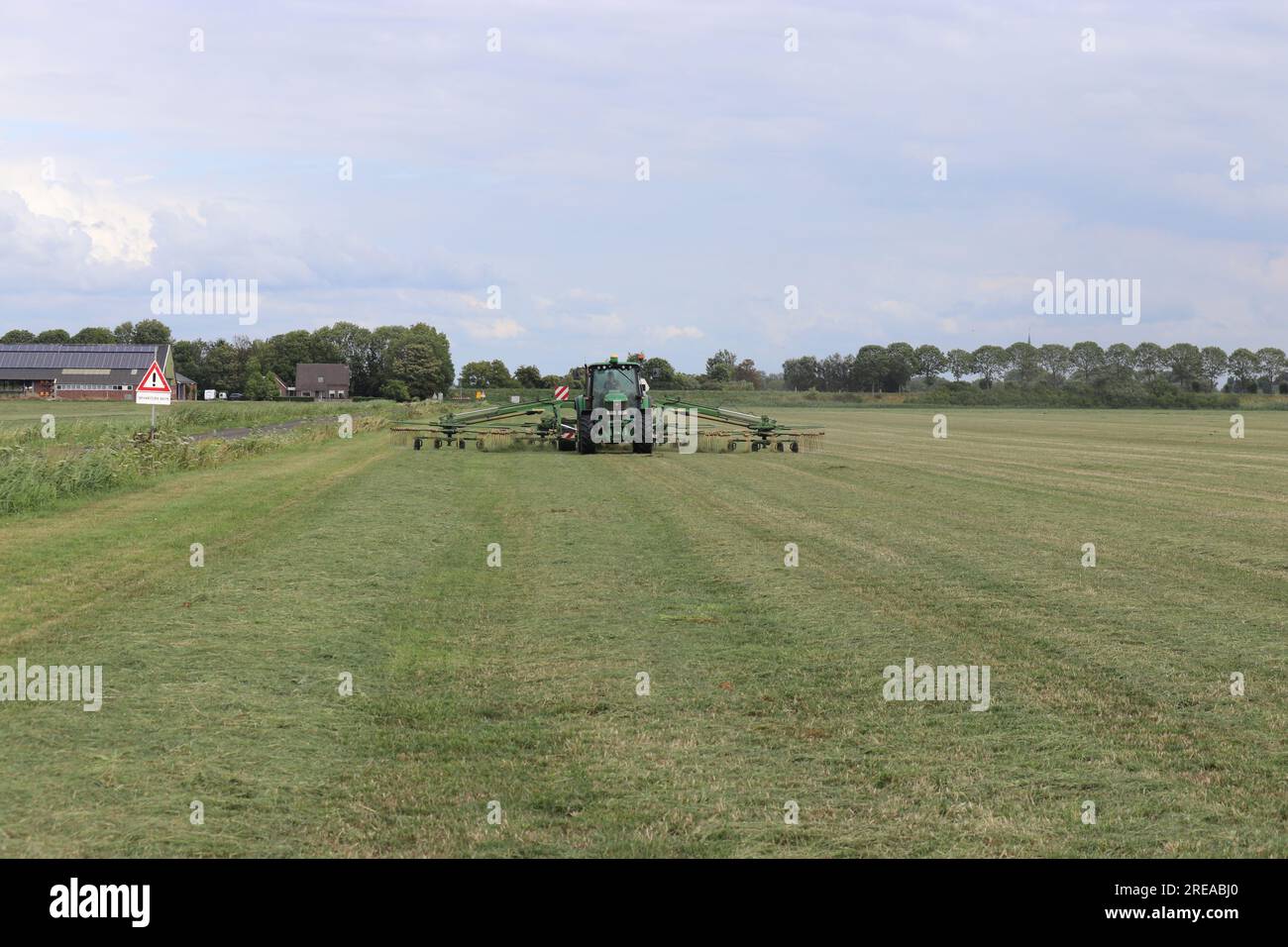 a field with green grass with a tractor with a big hay rake that is ...