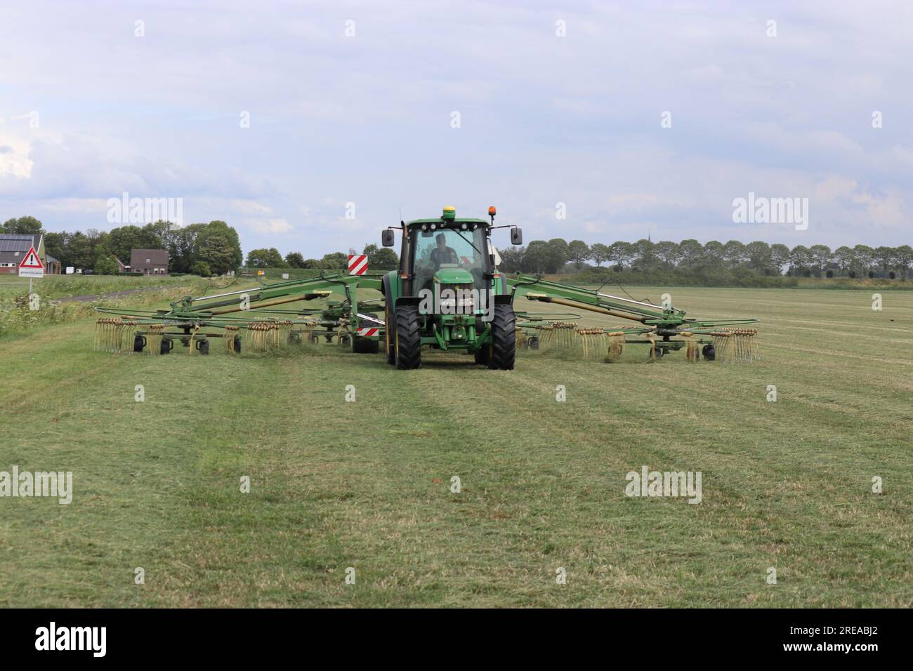 a tractor with a big hay rake is making rows of grass at a large green ...
