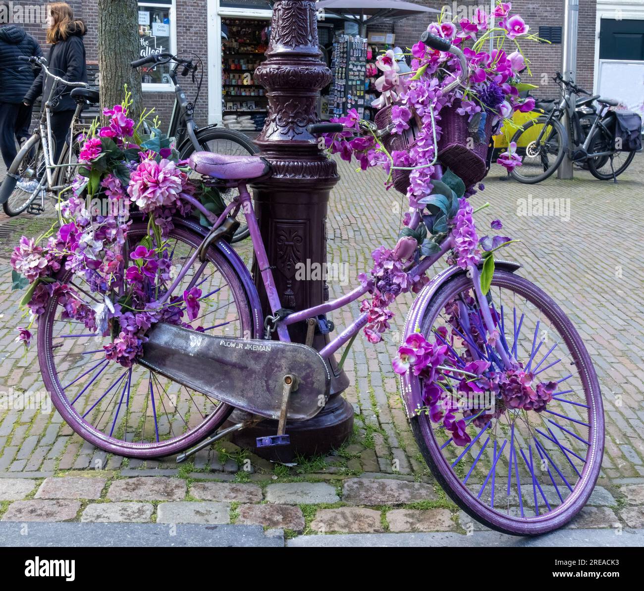 Purple decorated bicycle with purple flowers leaning against a lamppost ...