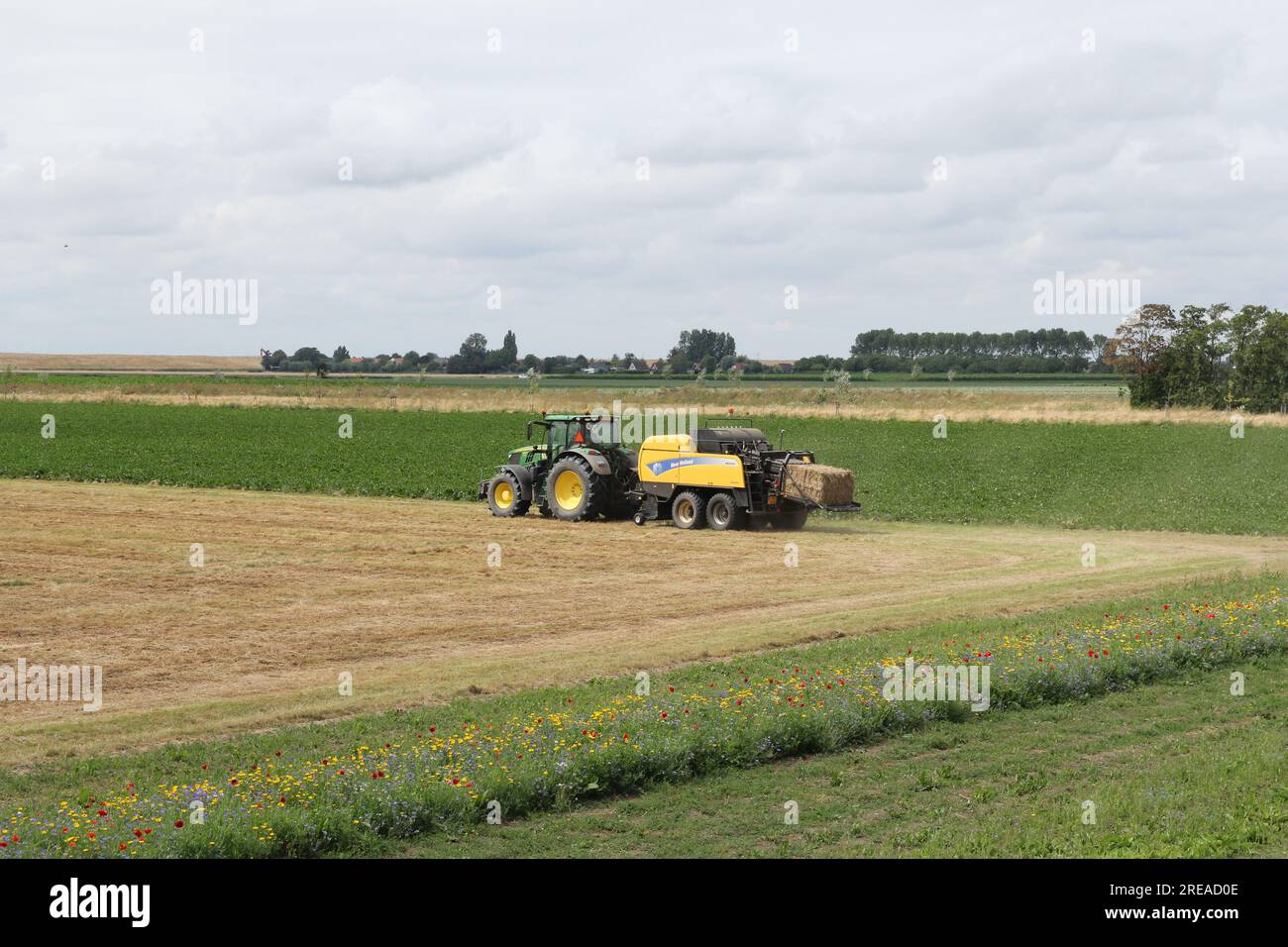 a rural landscape with a big baler at a yellow stubble field and a ...