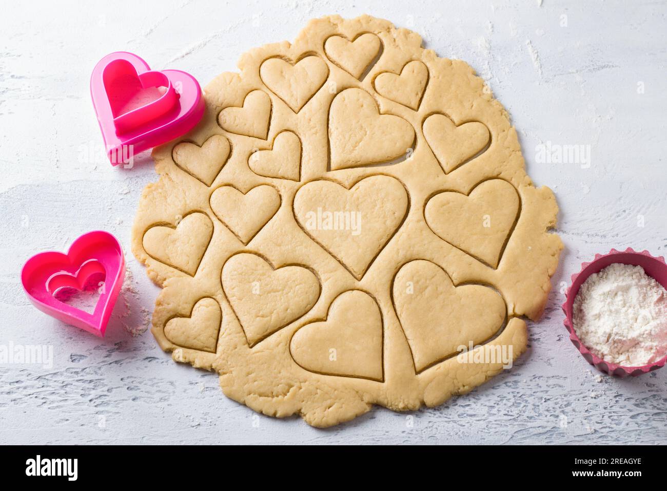 Cutting heart shaped cookies with cookie cutters on a light blue ...