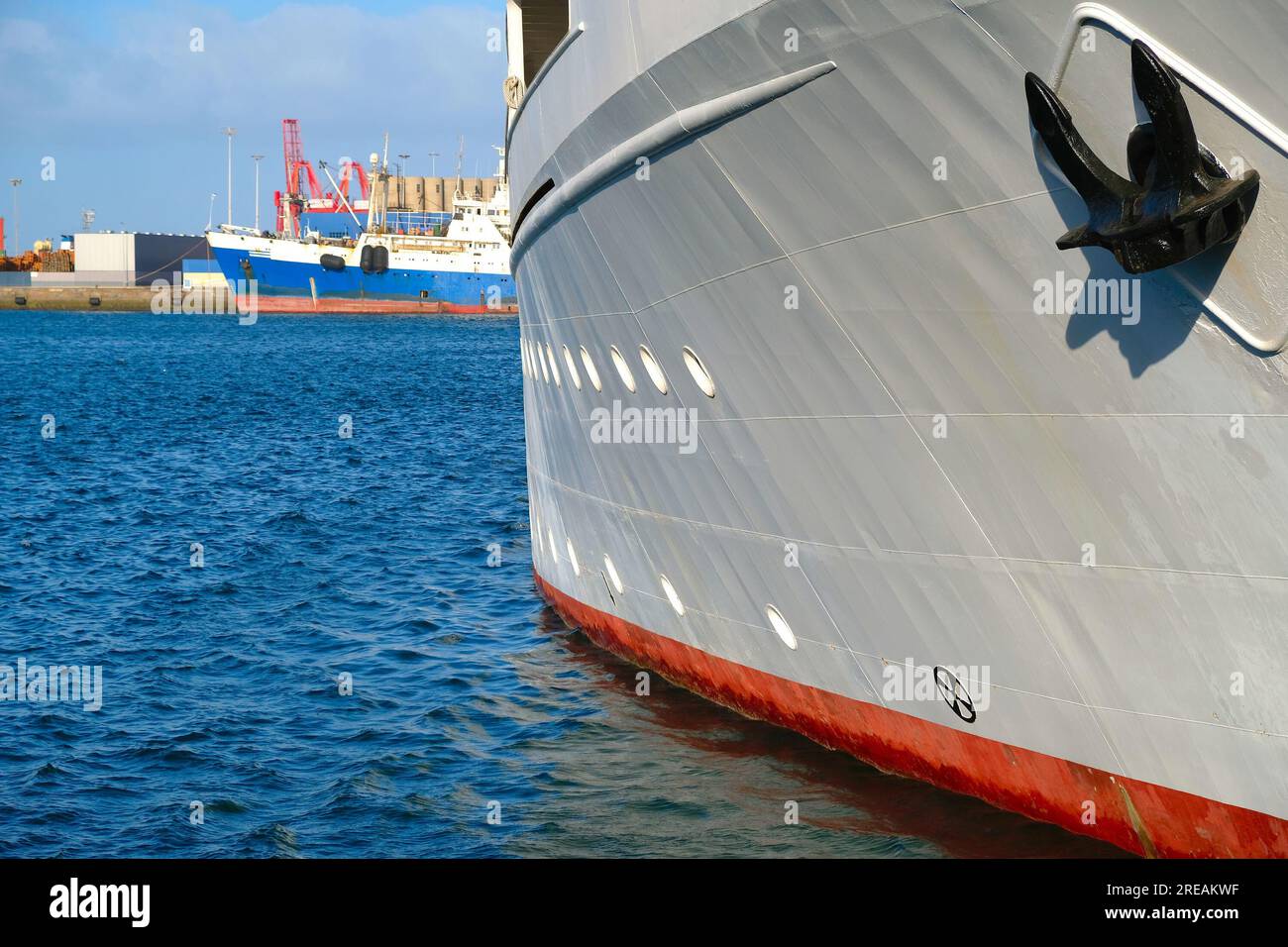 Starboard bow side of a white ship, with black anchor and blue habror ...