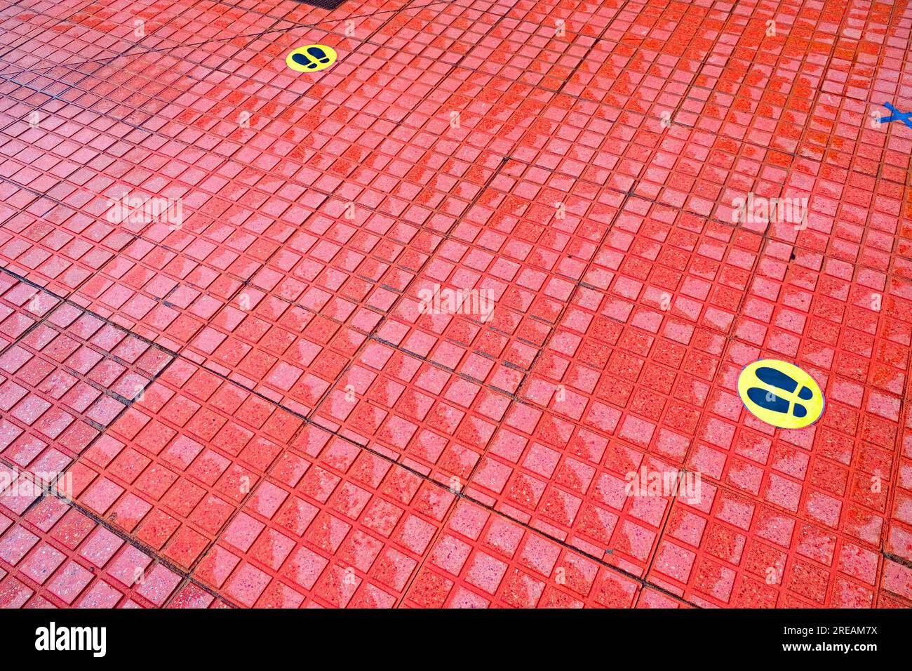 Wet red pavement and a signs with two black footprints in a yellow ...