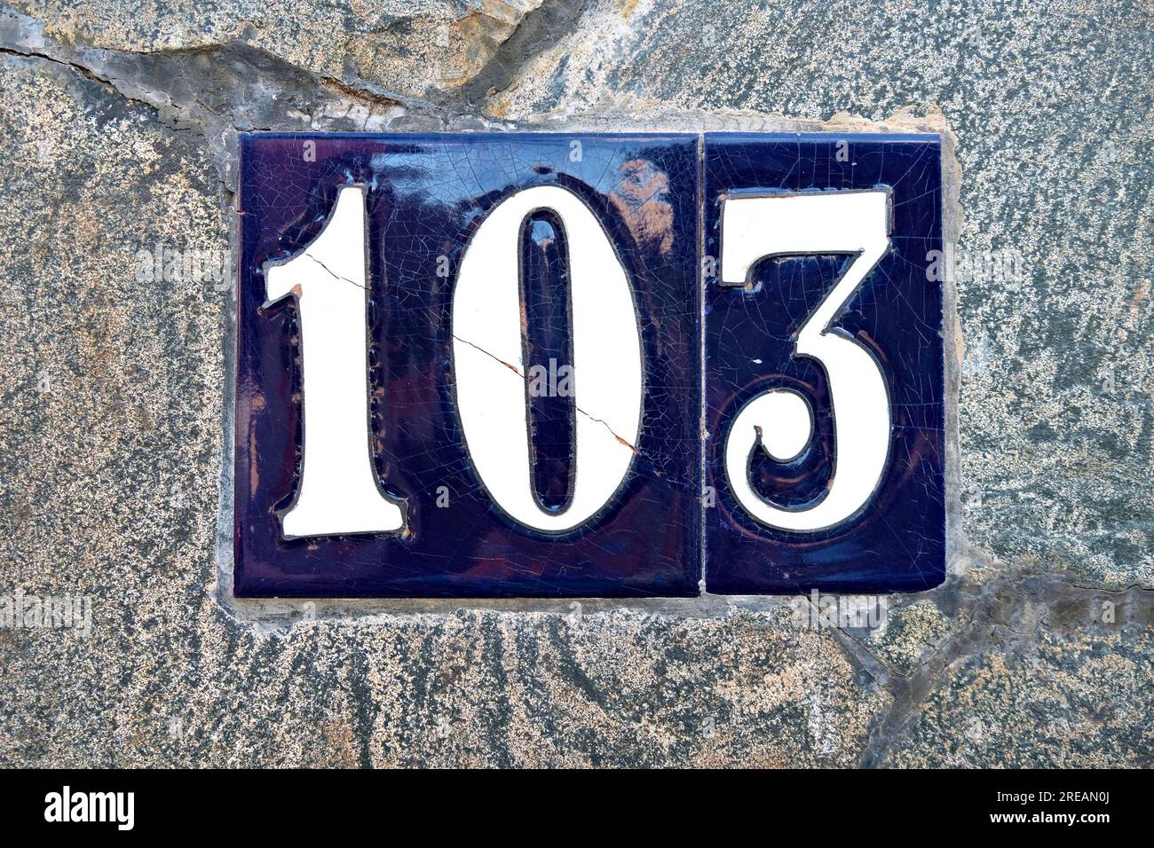 Number 103, one hundred and three, digits on blue tiles on a stone ...
