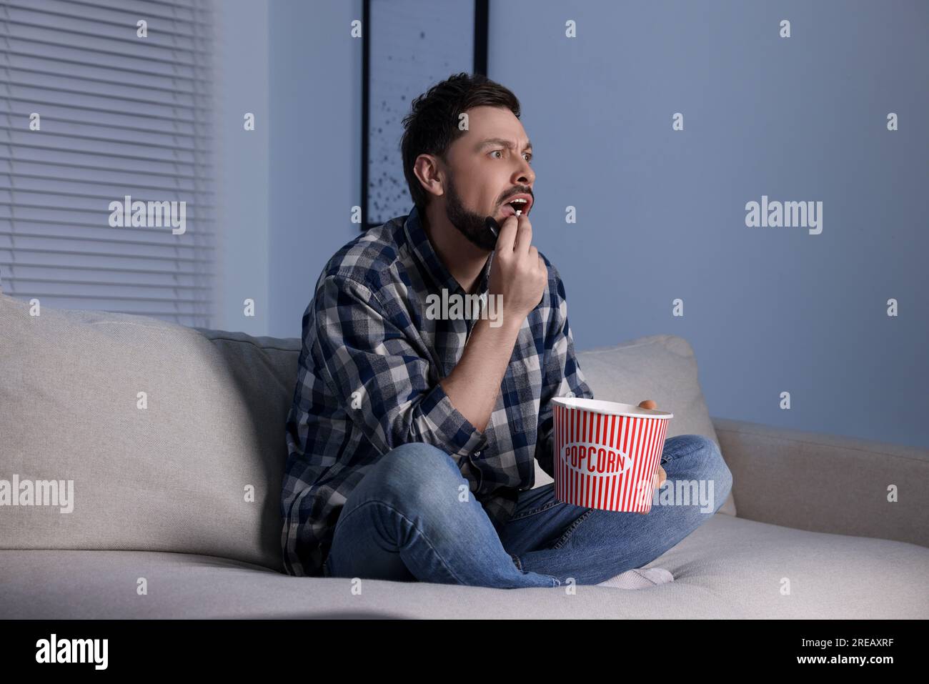 Emotional man eating popcorn while watching TV at home in evening Stock ...