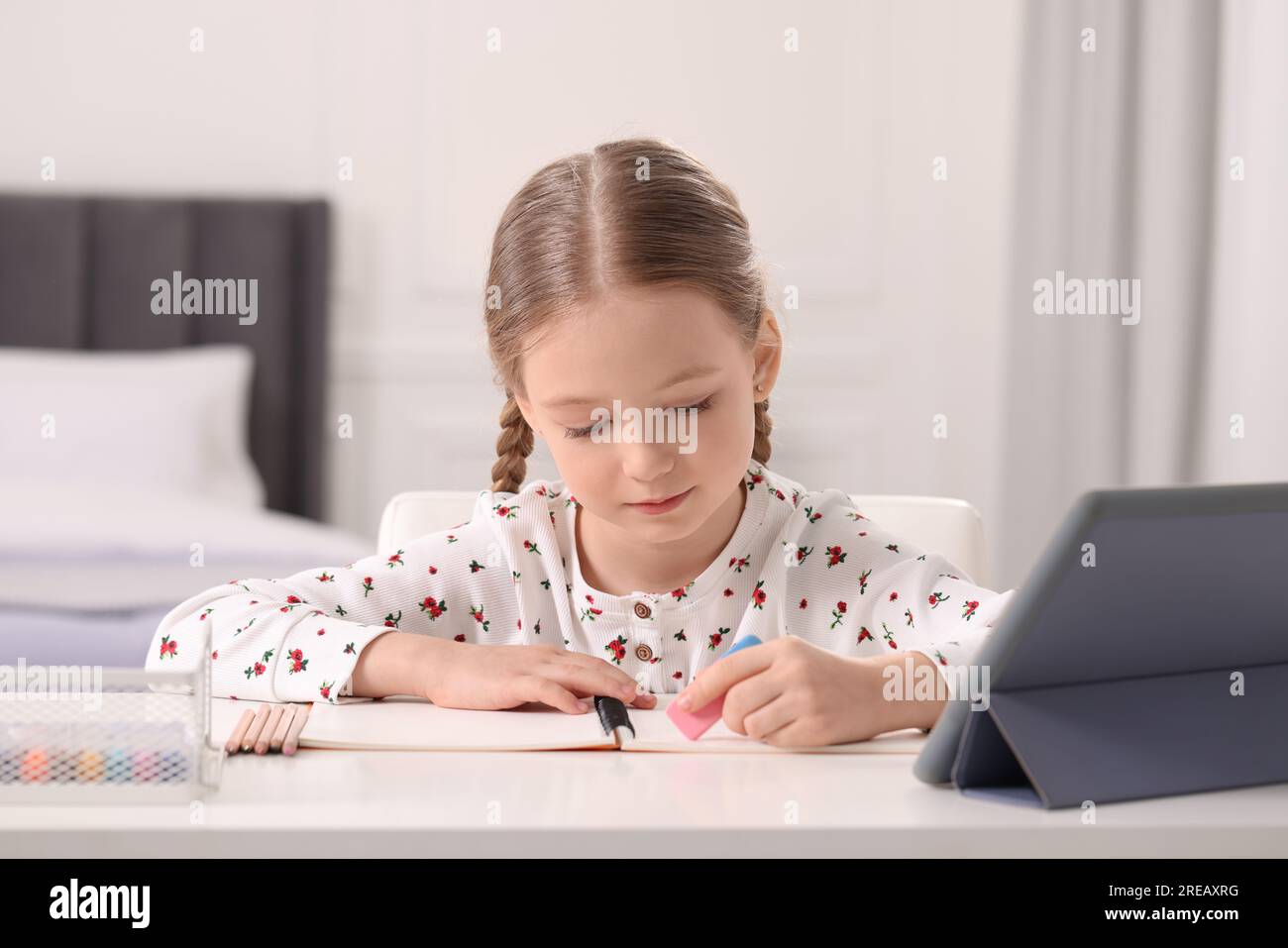 Girl using eraser at white desk in room Stock Photo - Alamy