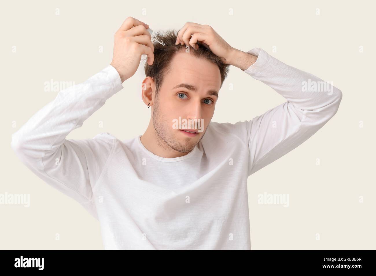 Young man using serum for hair growth on white background Stock Photo ...