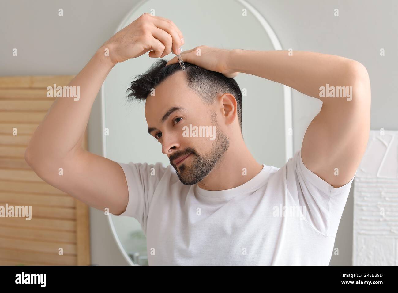 Handsome man using serum for hair growth in bathroom Stock Photo - Alamy