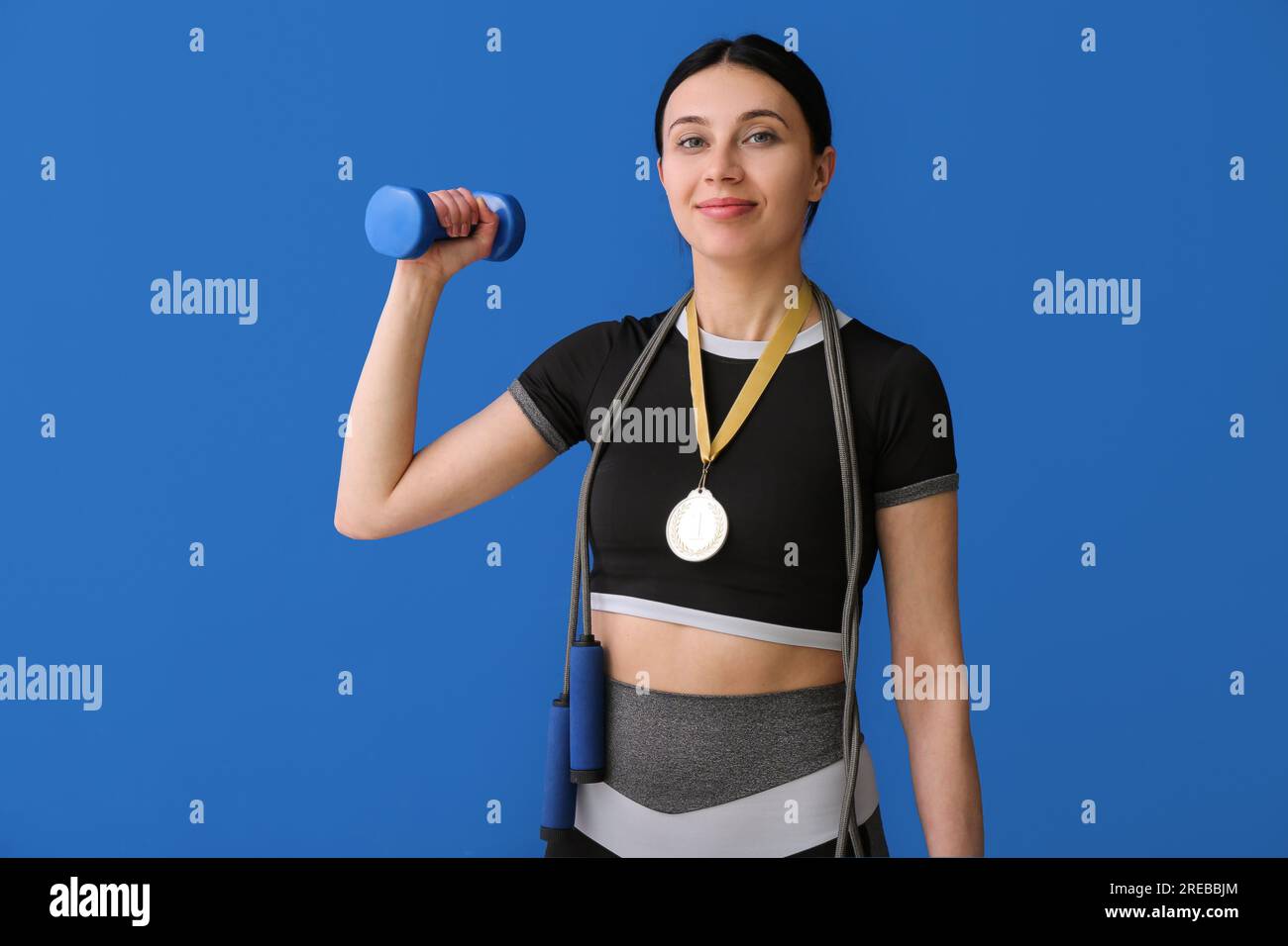 Sporty young woman with first place medal, skipping rope and dumbbell ...