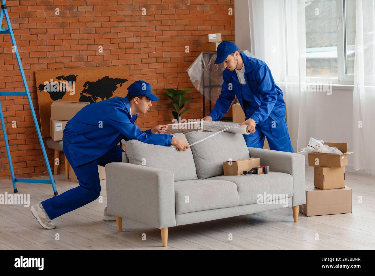 Male movers wrapping sofa with stretch film in room Stock Photo - Alamy