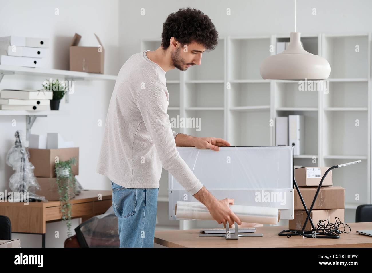 Young man wrapping computer monitor with stretch film in office Stock ...