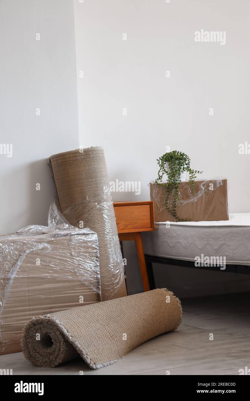 Cardboard boxes with rolled carpets and bed in room on moving day Stock ...