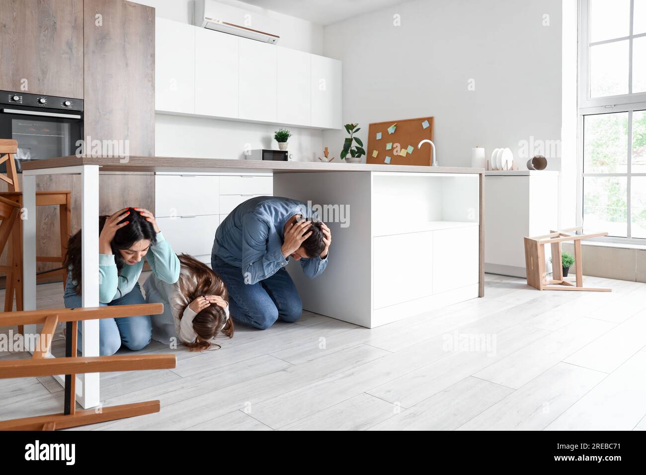 Scared family hiding under dining table during earthquake in kitchen ...